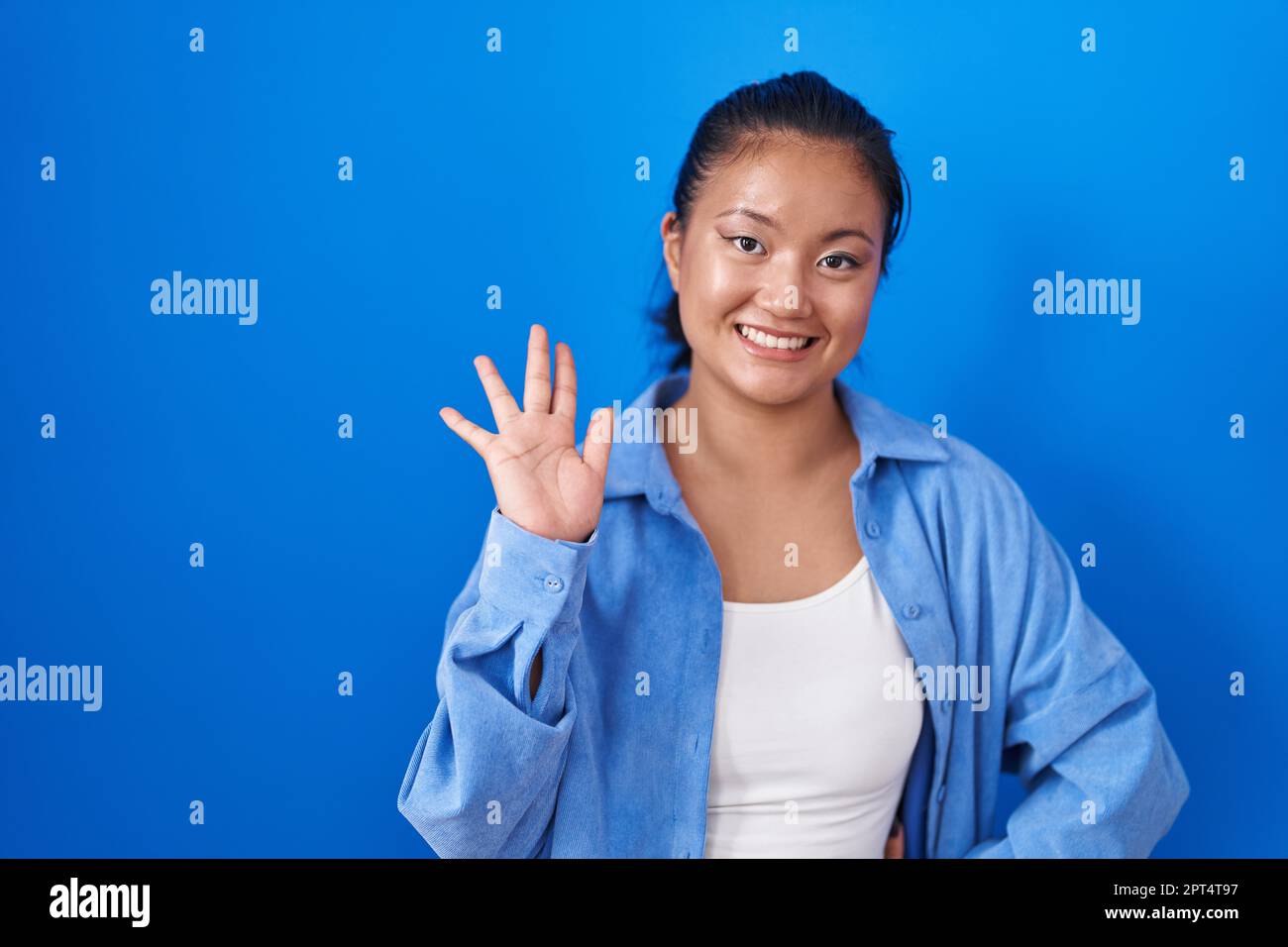 Asian Young Woman Standing Over Blue Background Waiving Saying Hello