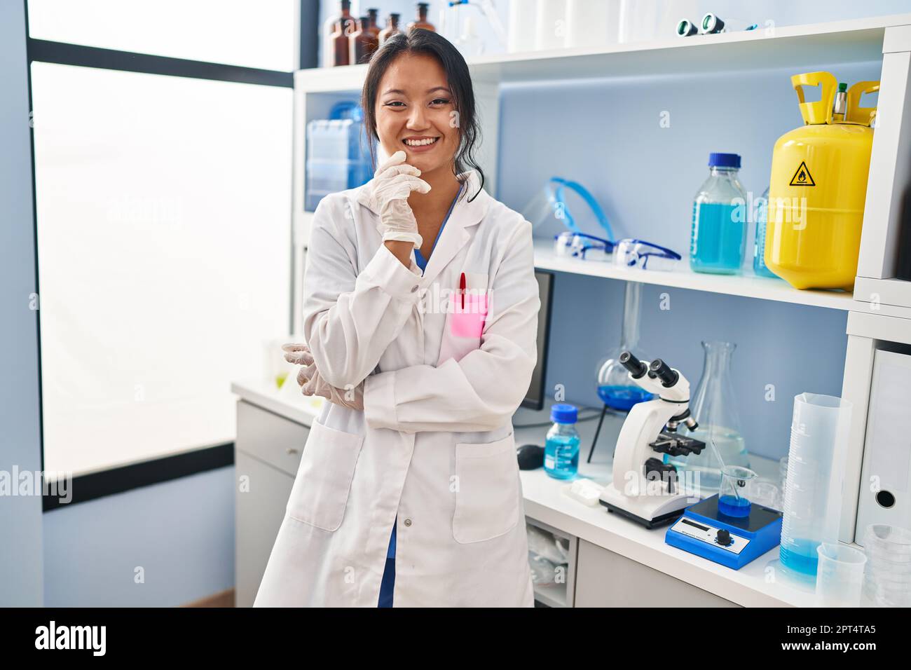 Young chinese woman wearing scientist uniform standing with arms ...