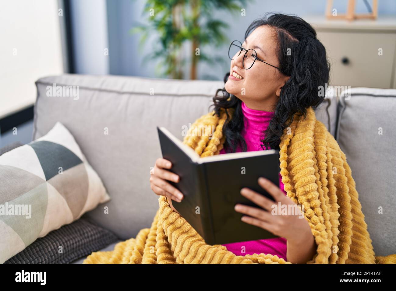 Young chinese woman reading book sitting on sofa at home Stock Photo ...