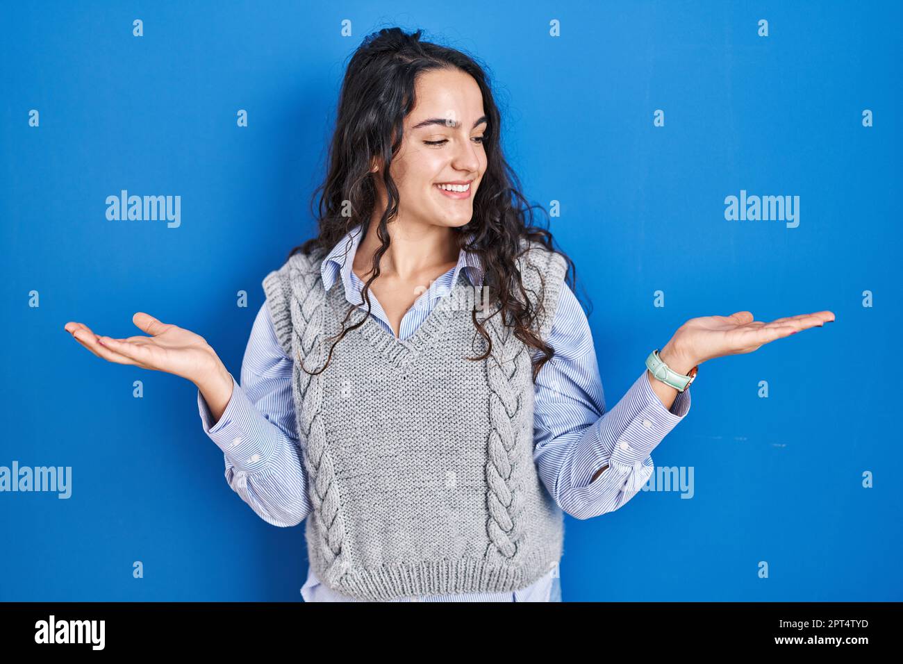Young brunette woman standing over blue background smiling showing both ...