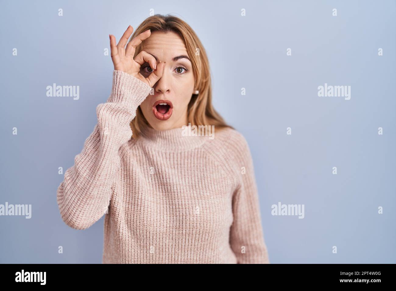 Hispanic woman standing over blue background doing ok gesture shocked ...