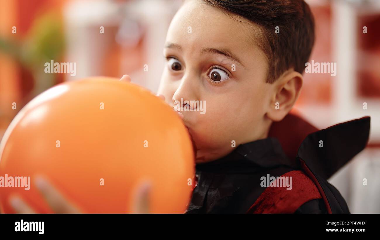 Adorable hispanic boy wearing halloween costume inflating balloon at ...