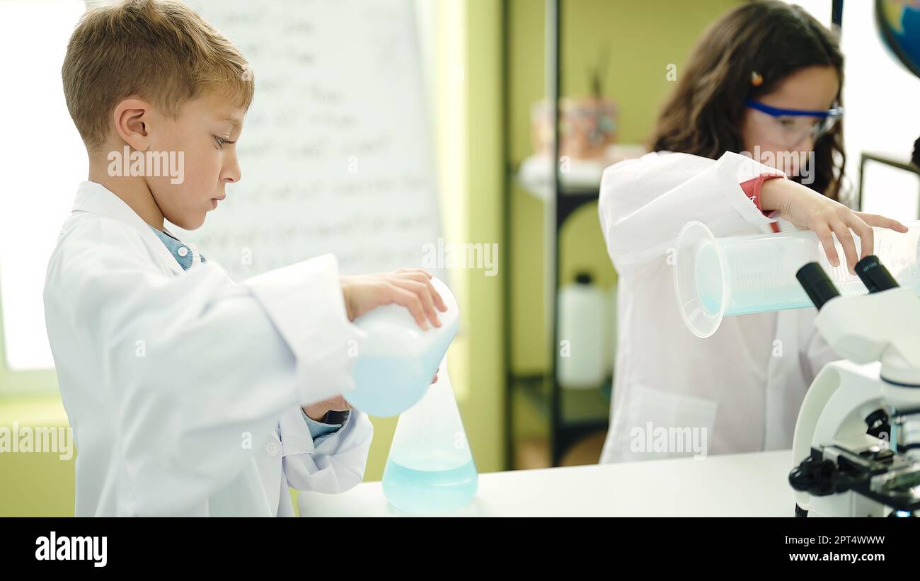 Adorable boy and girl student pouring liquid on test tube at laboratory ...
