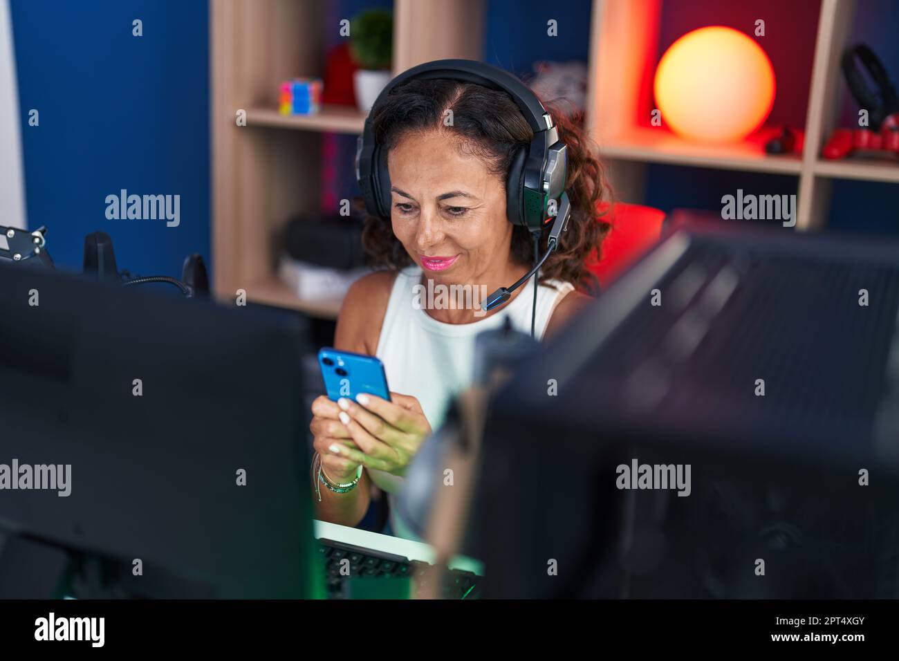 Middle age woman streamer using computer and smartphone at gaming room ...