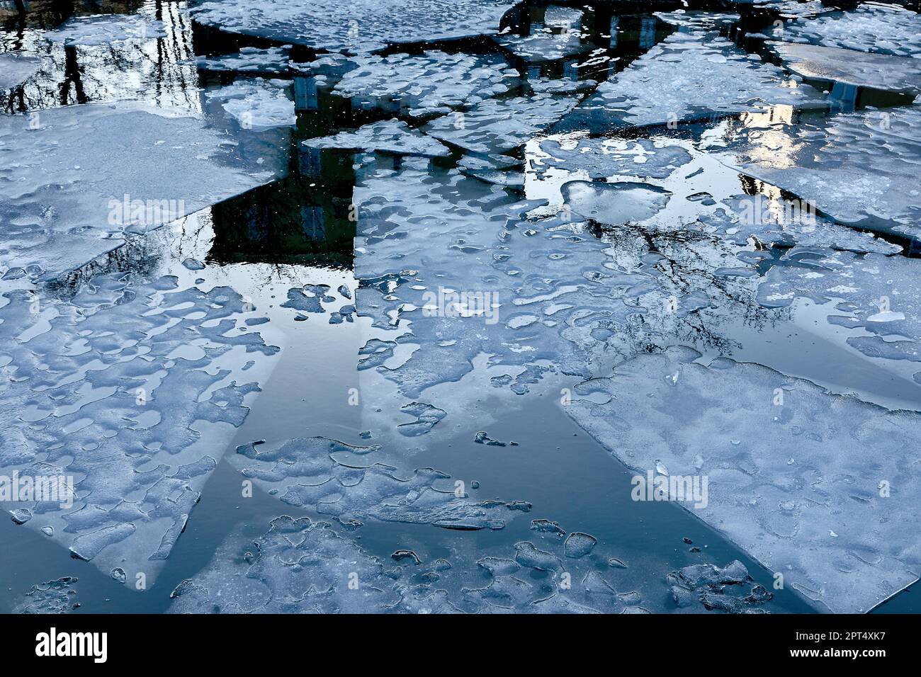 Ice sheets on a frozen water body with town building reflections in ...