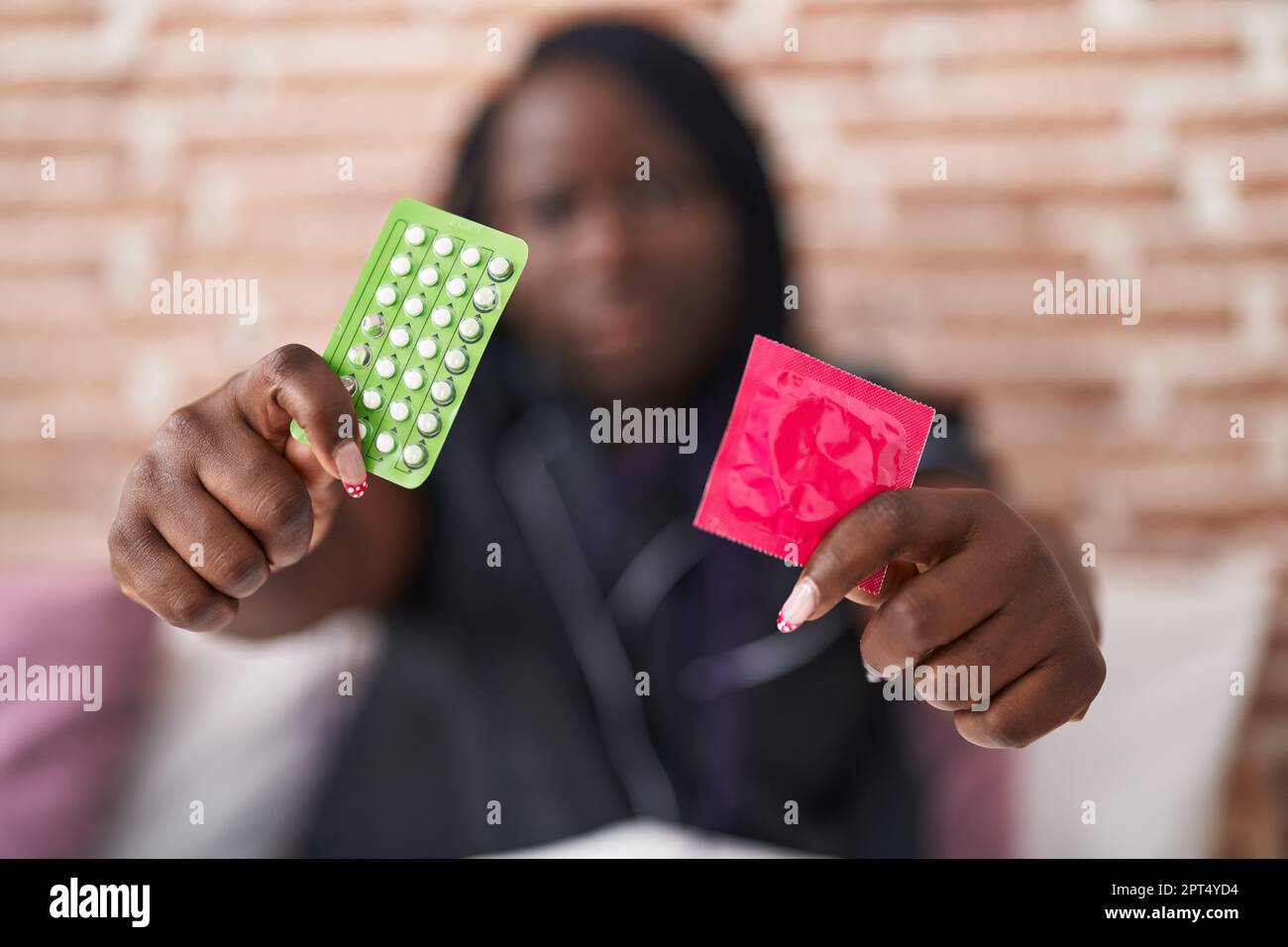 African american woman holding condom and birth control pills sitting ...