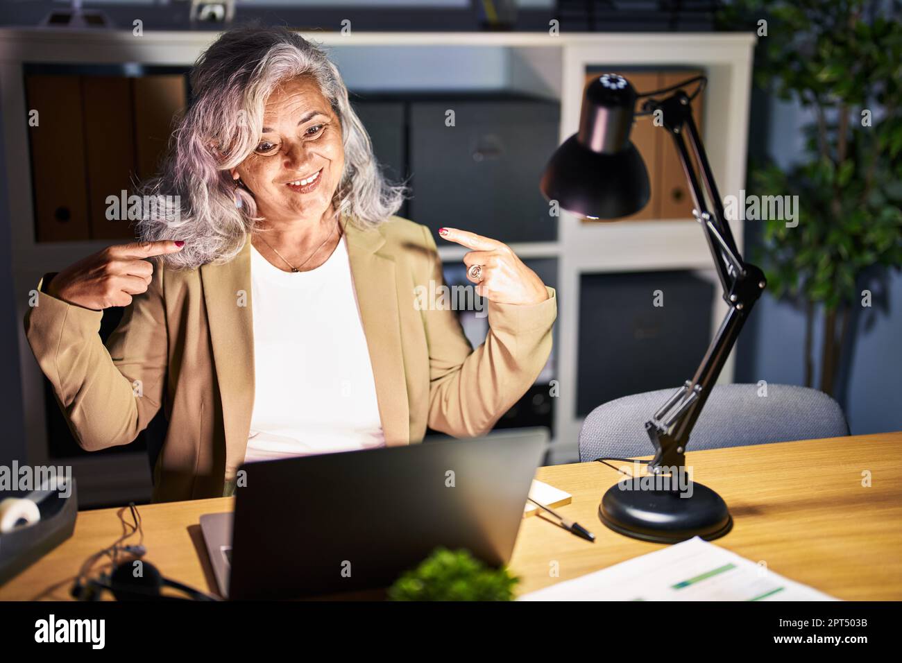 Middle age woman with grey hair working using computer laptop late at ...