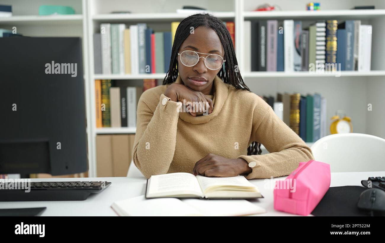 African woman reading a book sitting on desk at library university ...