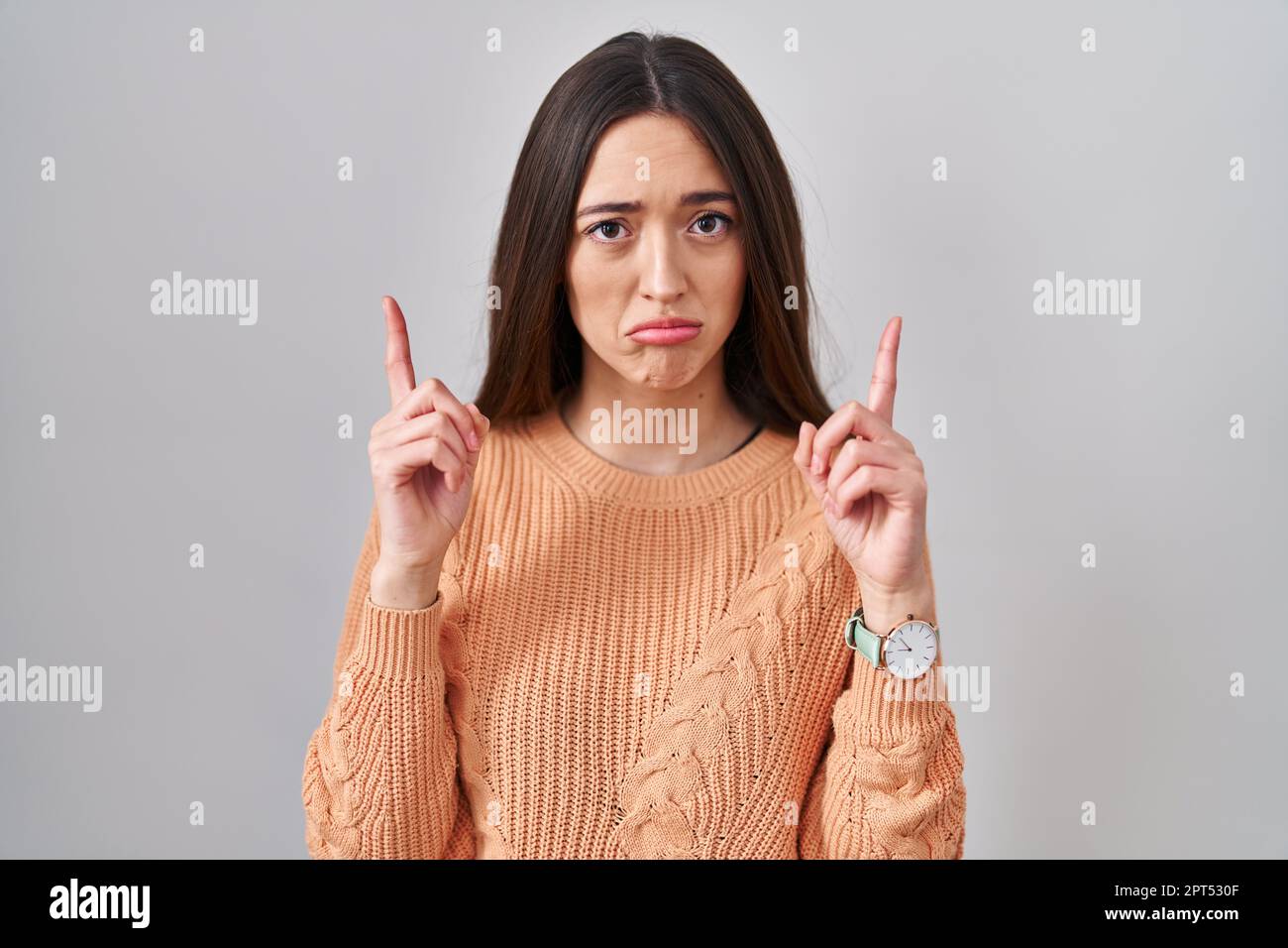 Young brunette woman standing over white background pointing up looking ...