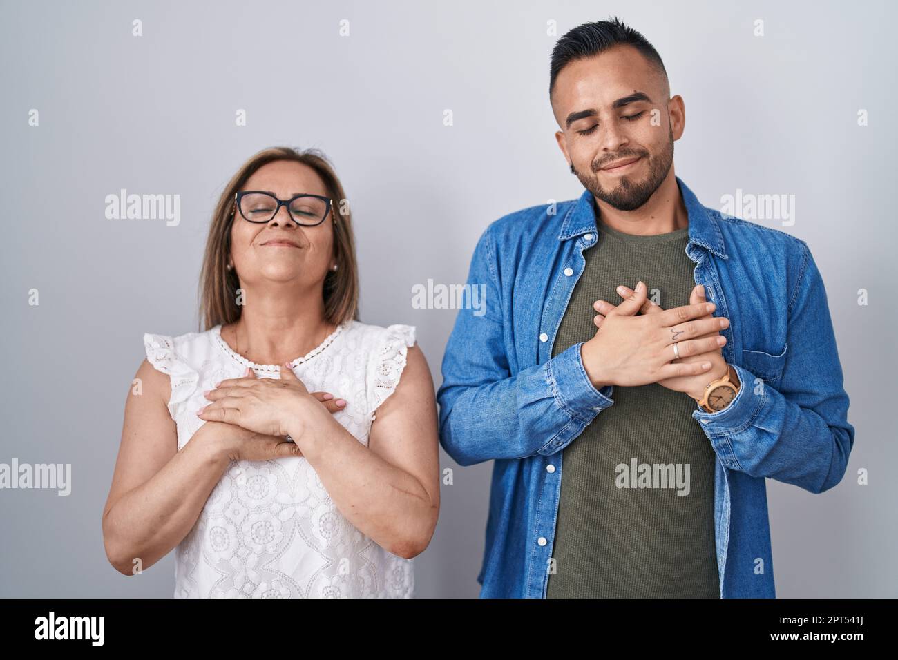 Hispanic mother and son standing together smiling with hands on chest ...