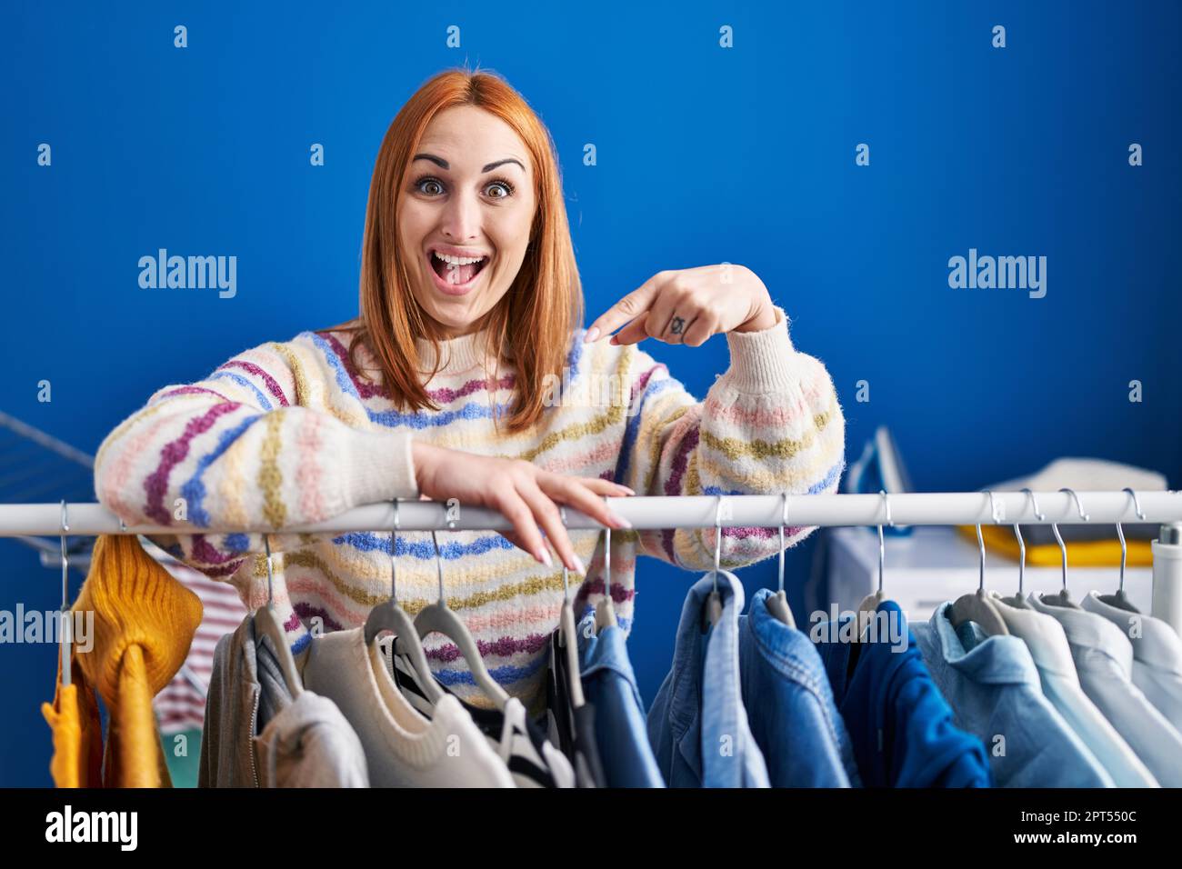 Young woman searching clothes on clothing rack smiling happy pointing ...