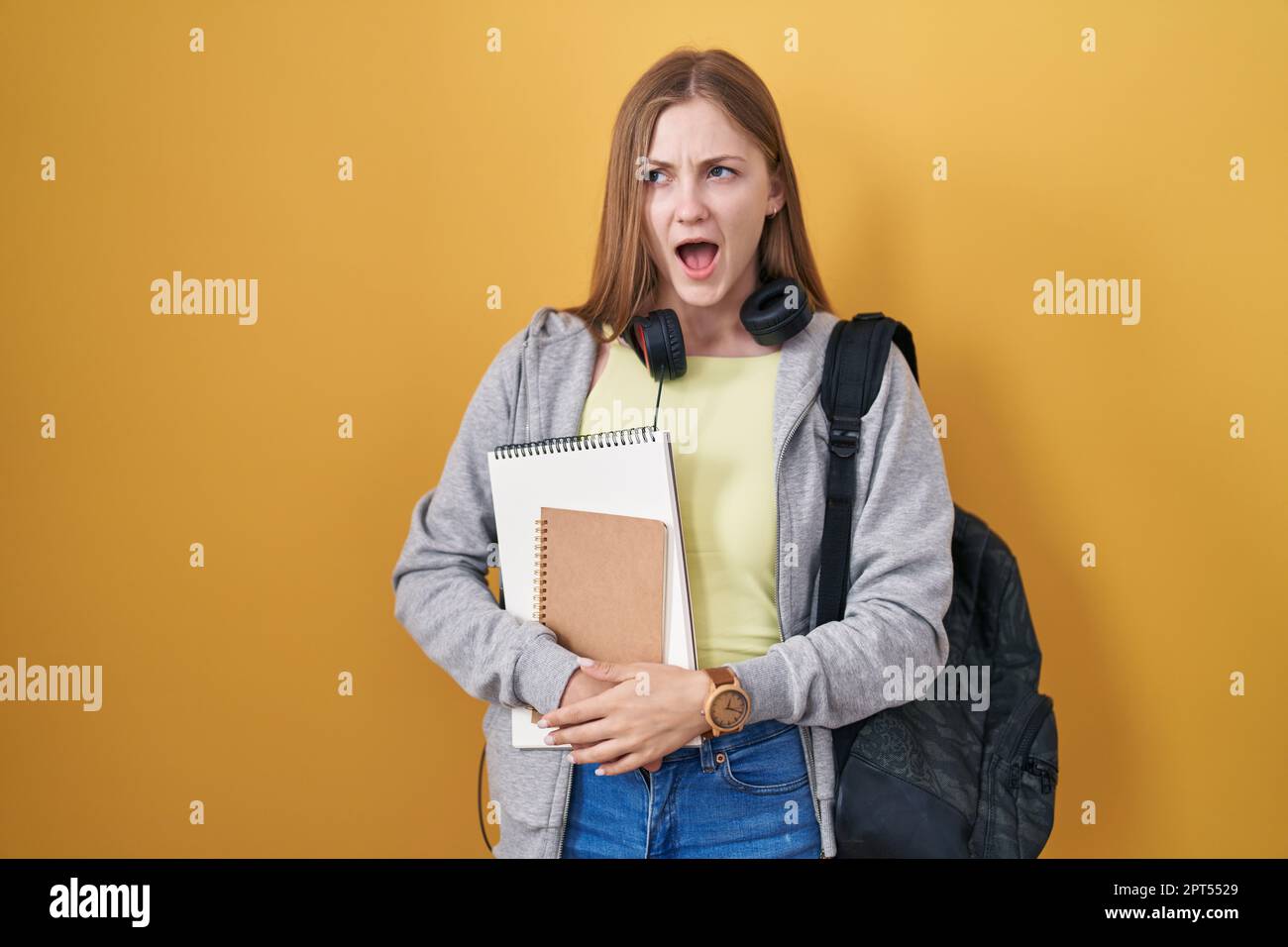 Young caucasian woman wearing student backpack and holding books angry ...