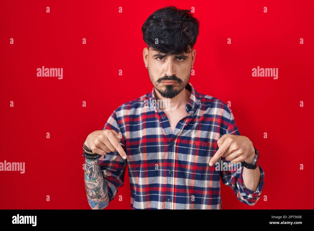Young hispanic man with beard standing over red background pointing ...
