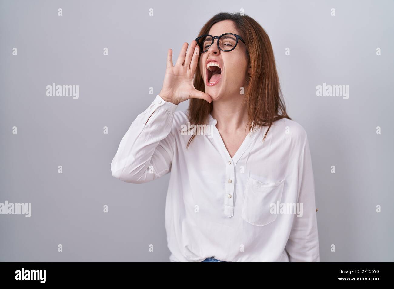 Brunette woman standing over white isolated background shouting and ...