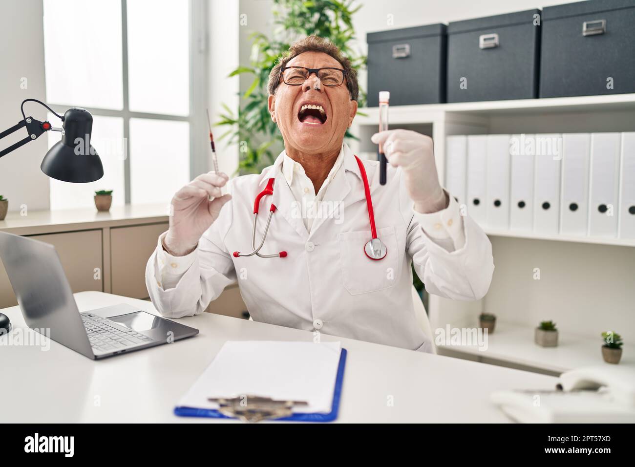 Senior doctor man holding syringe and blood sample angry and mad ...