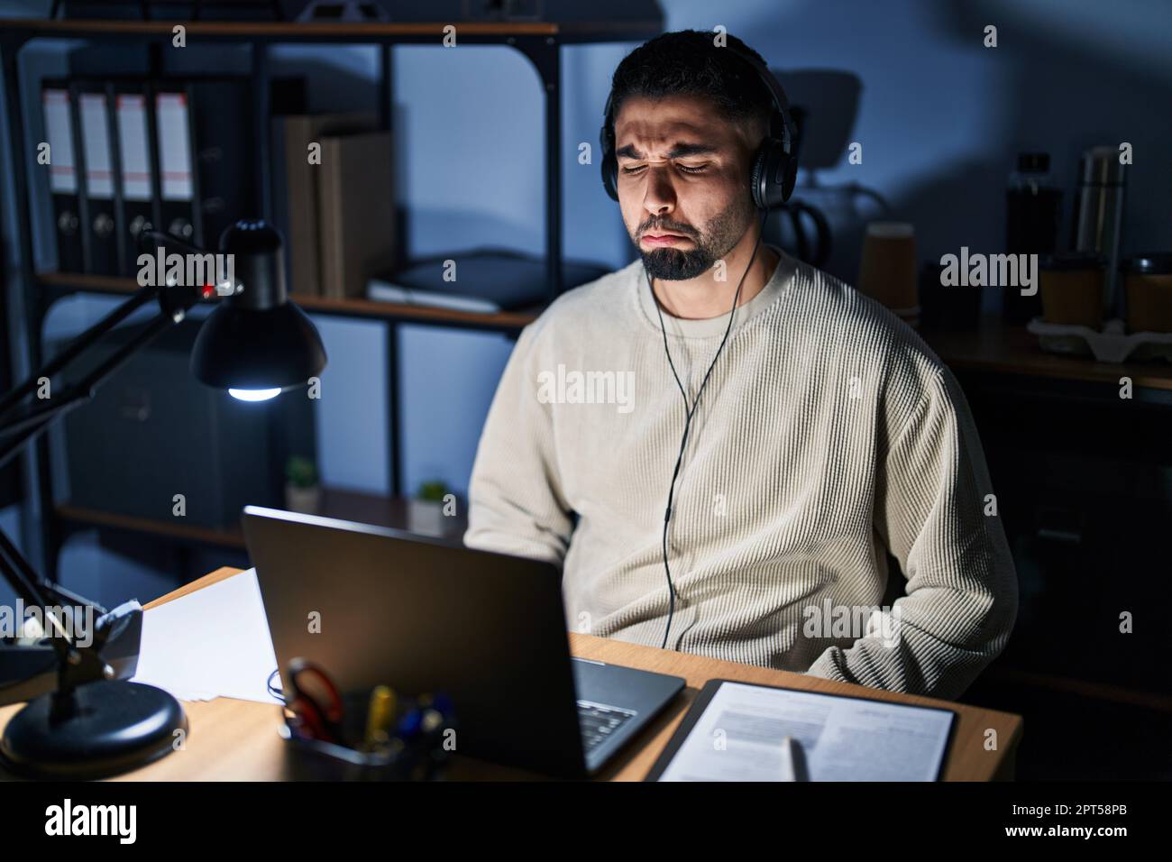 Young handsome man working using computer laptop at night depressed and ...