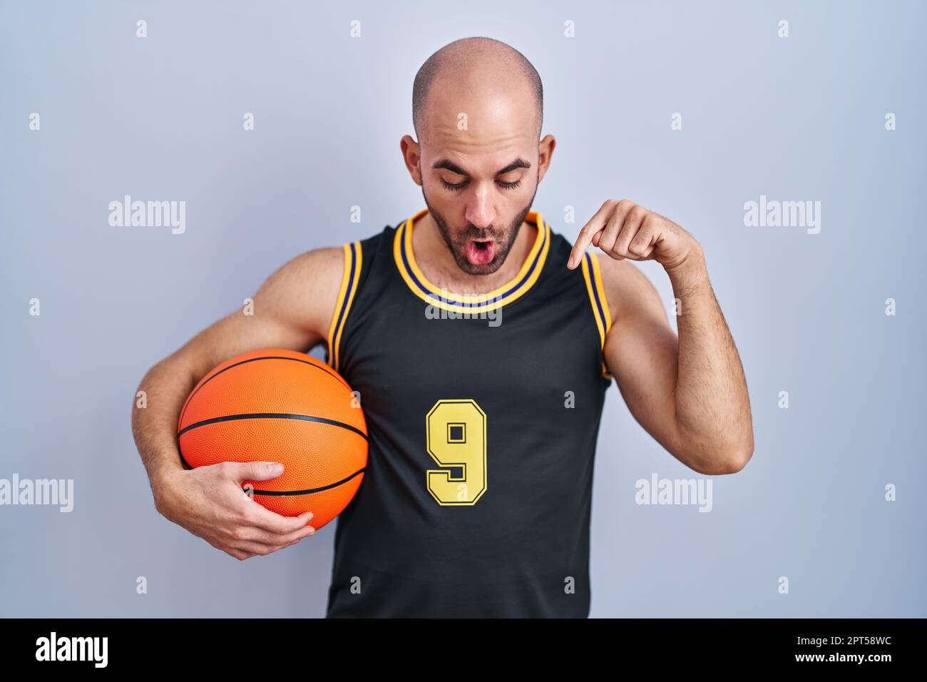 Young bald man with beard wearing basketball uniform holding ball ...