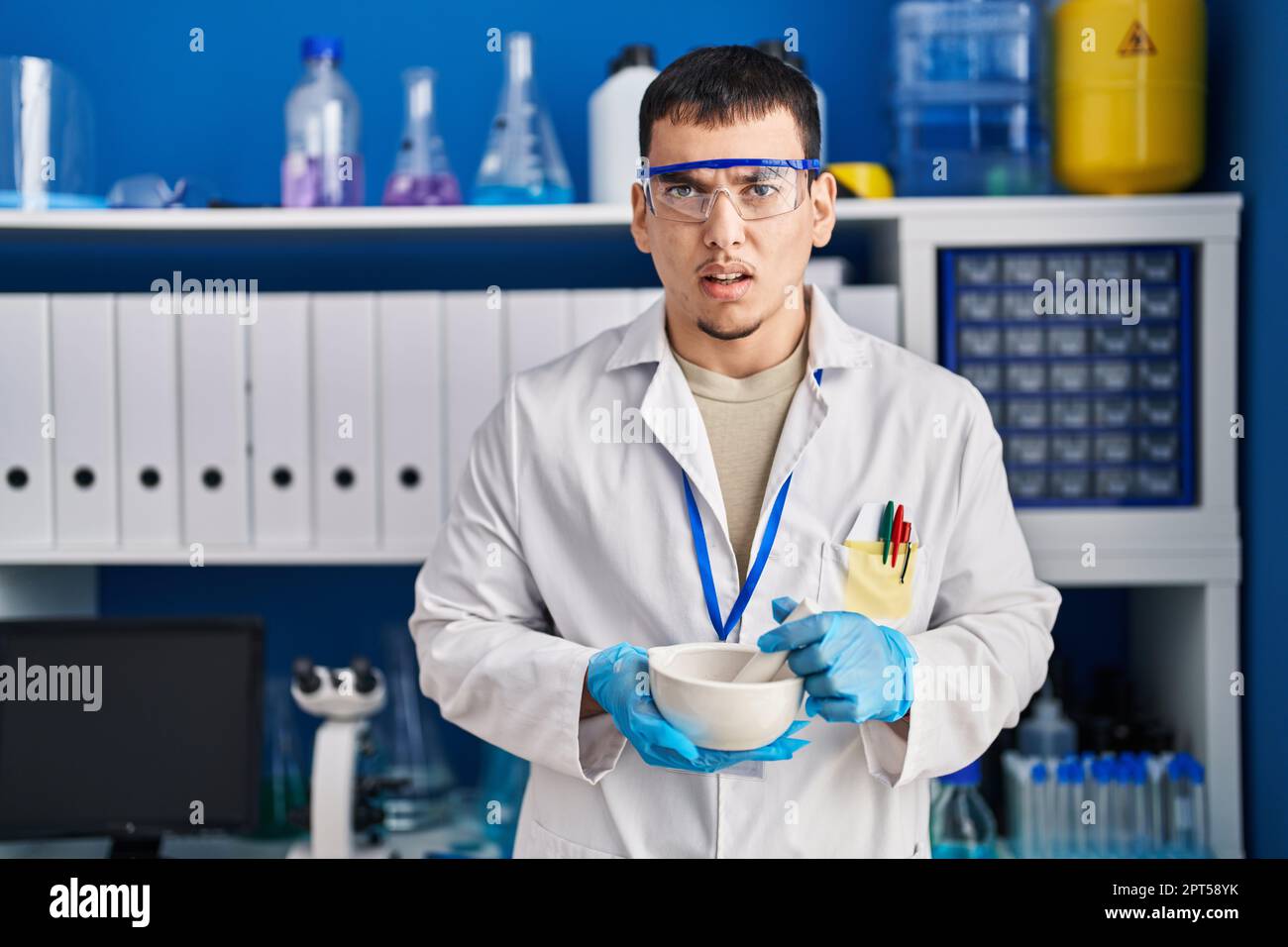 Young arab man working at scientist laboratory clueless and confused expression. doubt concept ...