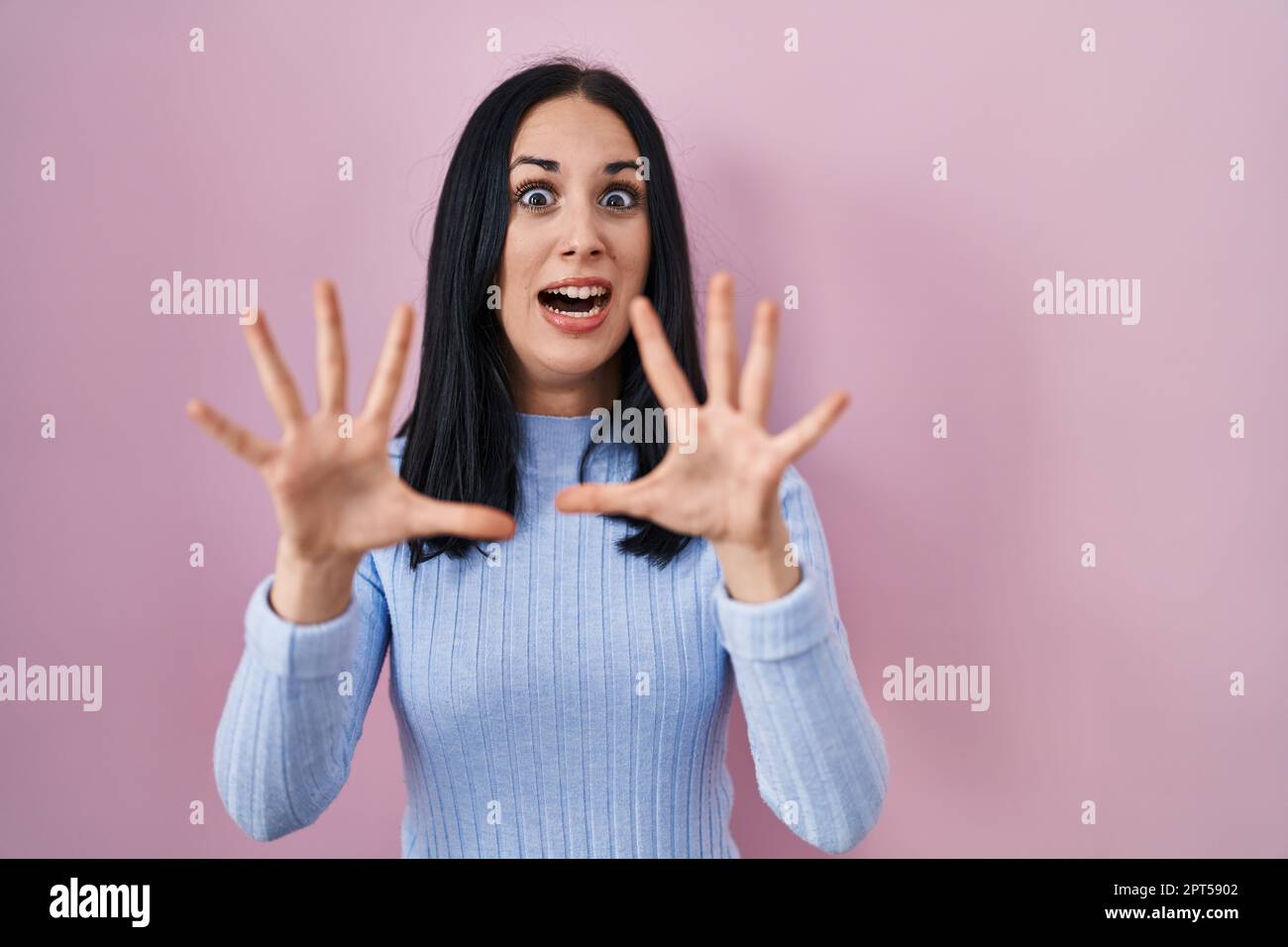 Hispanic woman standing over pink background afraid and terrified with ...
