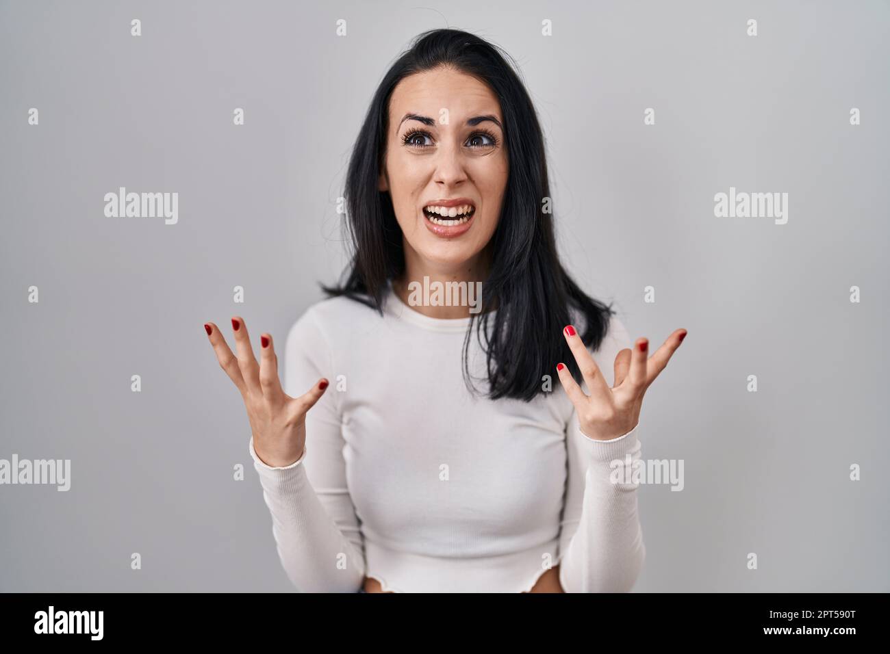 Hispanic woman standing over isolated background crazy and mad shouting ...