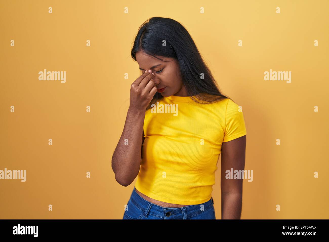 Young indian woman standing over yellow background tired rubbing nose ...