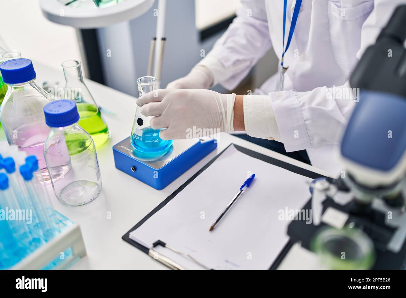 Young hispanic man scientist measuring liquid writing report at ...