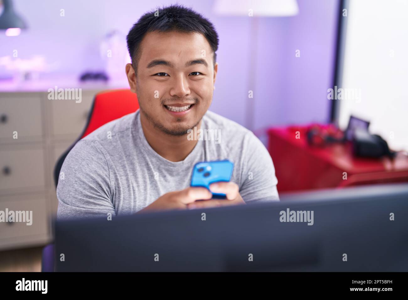 Young chinese man streamer using computer and smartphone at gaming room ...