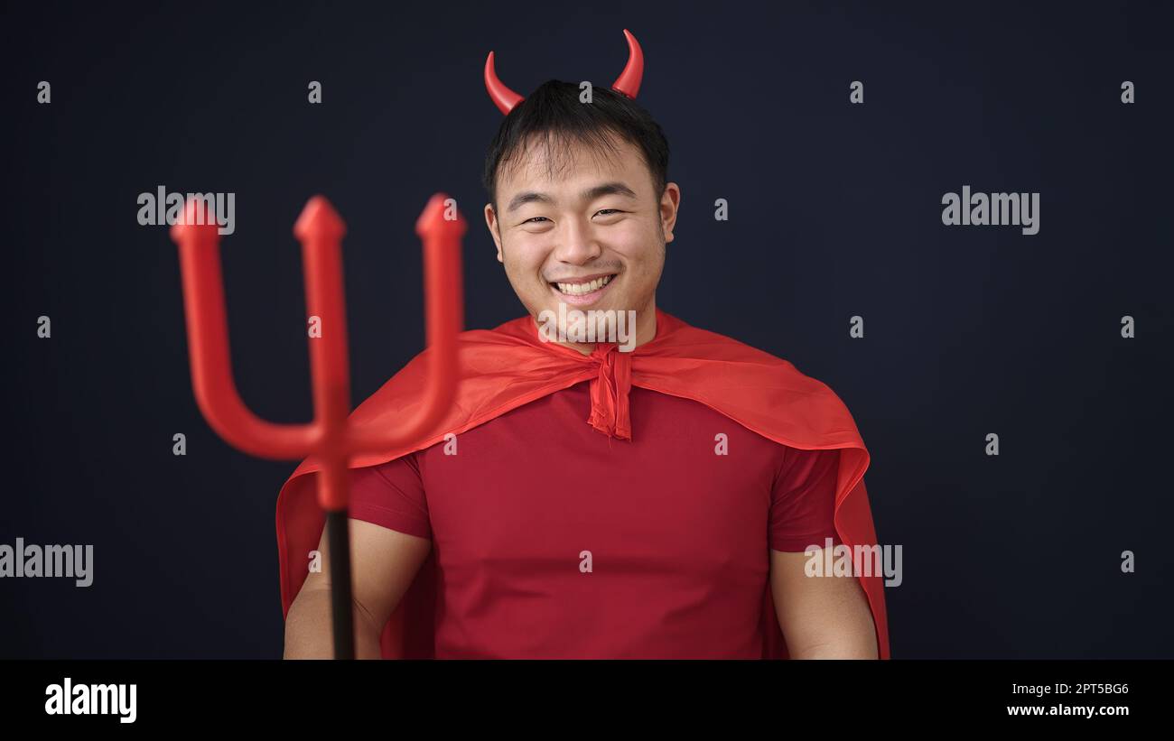Young chinese man wearing devil costume holding trident over isolated ...