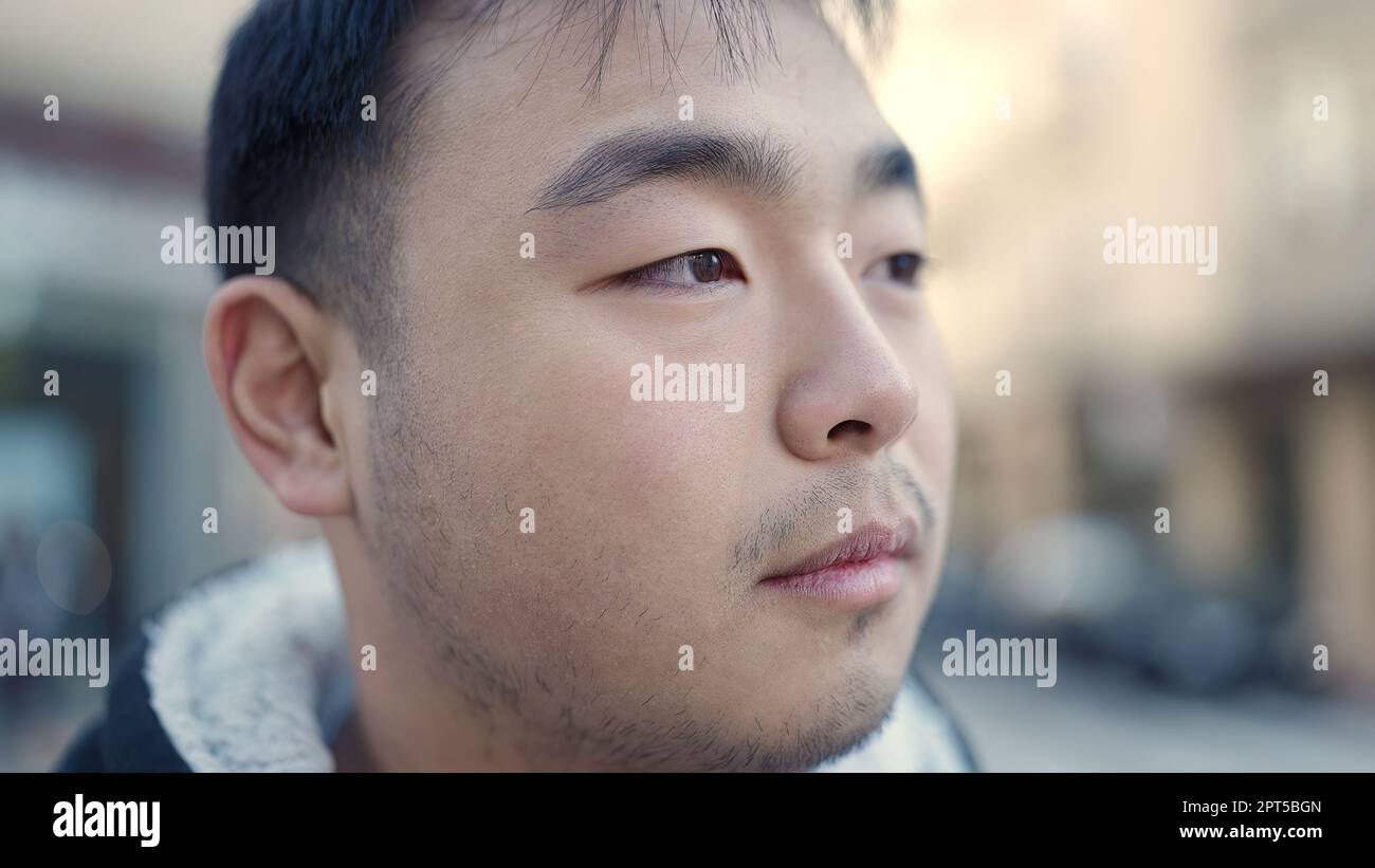 Young chinese man looking to the side with serious expression at street ...