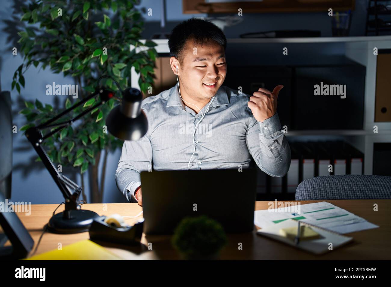 Young chinese man working using computer laptop at night smiling with ...
