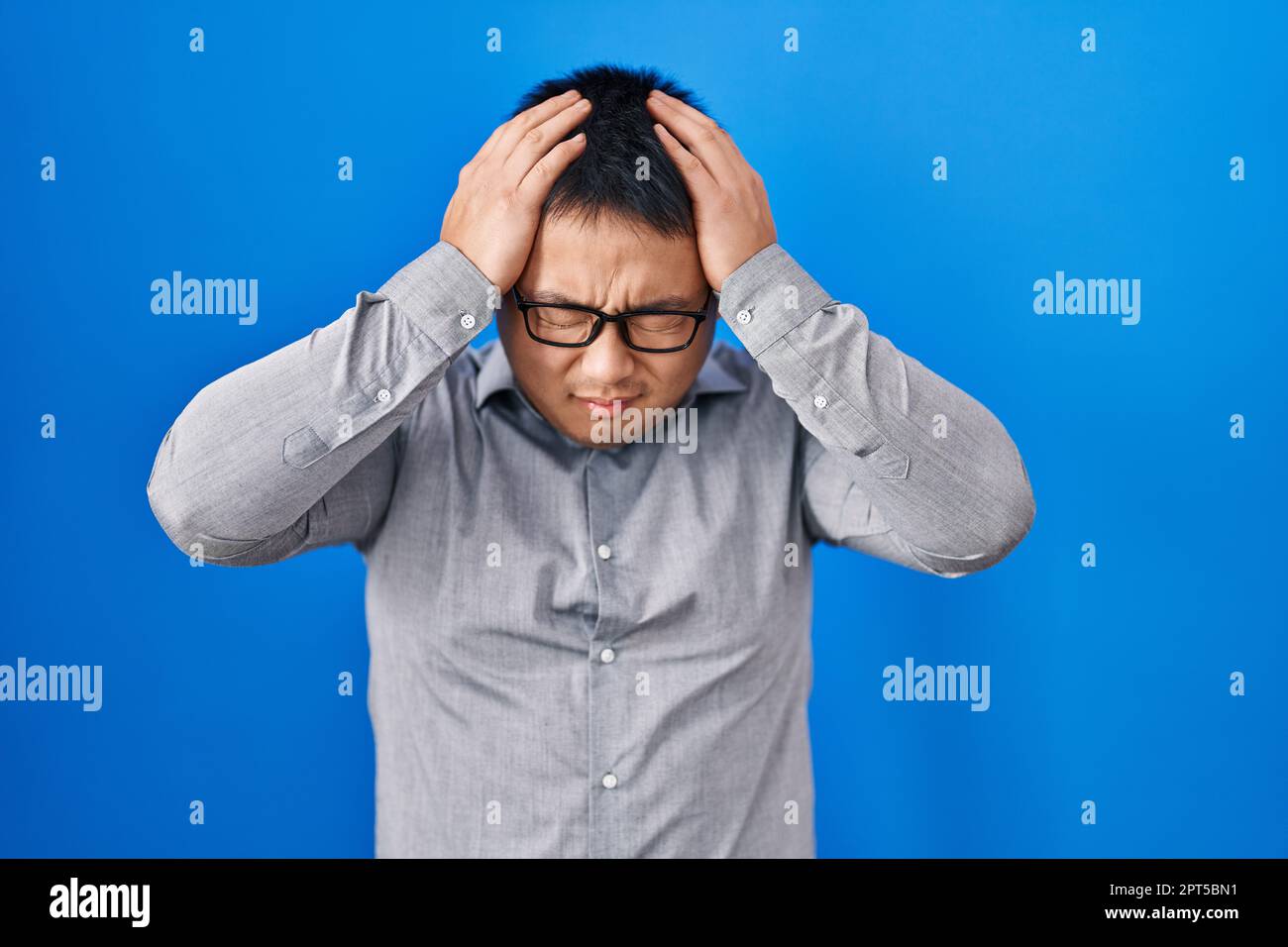 Young chinese man standing over blue background suffering from headache ...