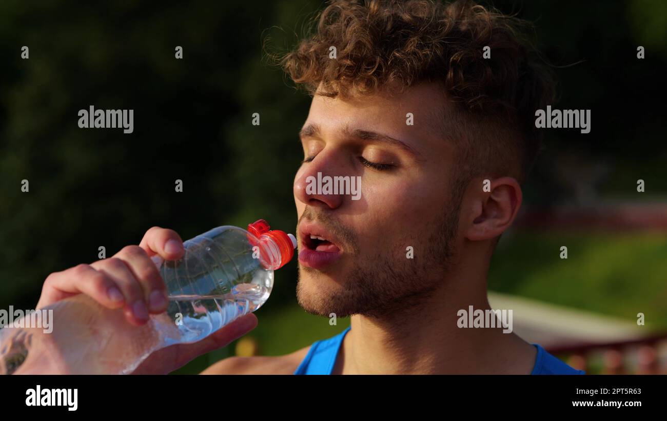 Handsome young sportsman with serious face drinking water from bottle ...