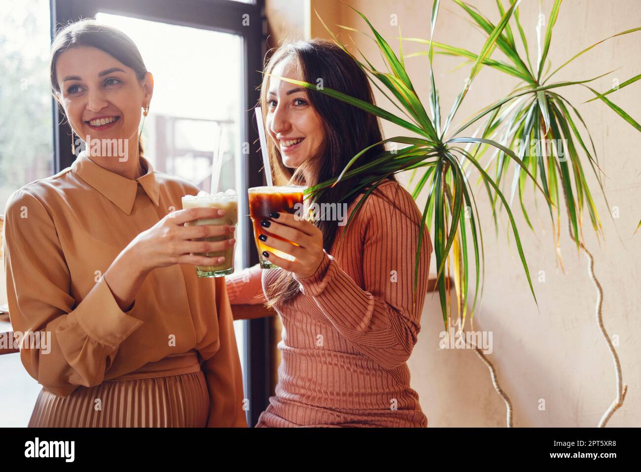 Happy young female friends having coffee break while relaxing at indoor ...