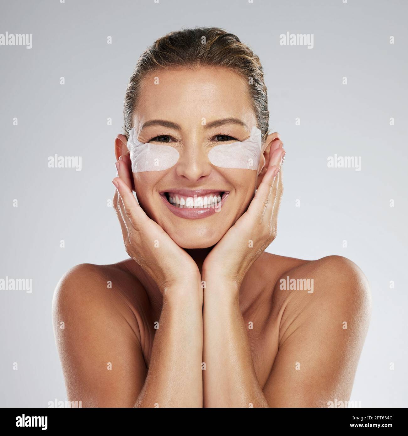 Skincare, portrait and woman doing face cosmetics, smile and makeup with grey studio background ...