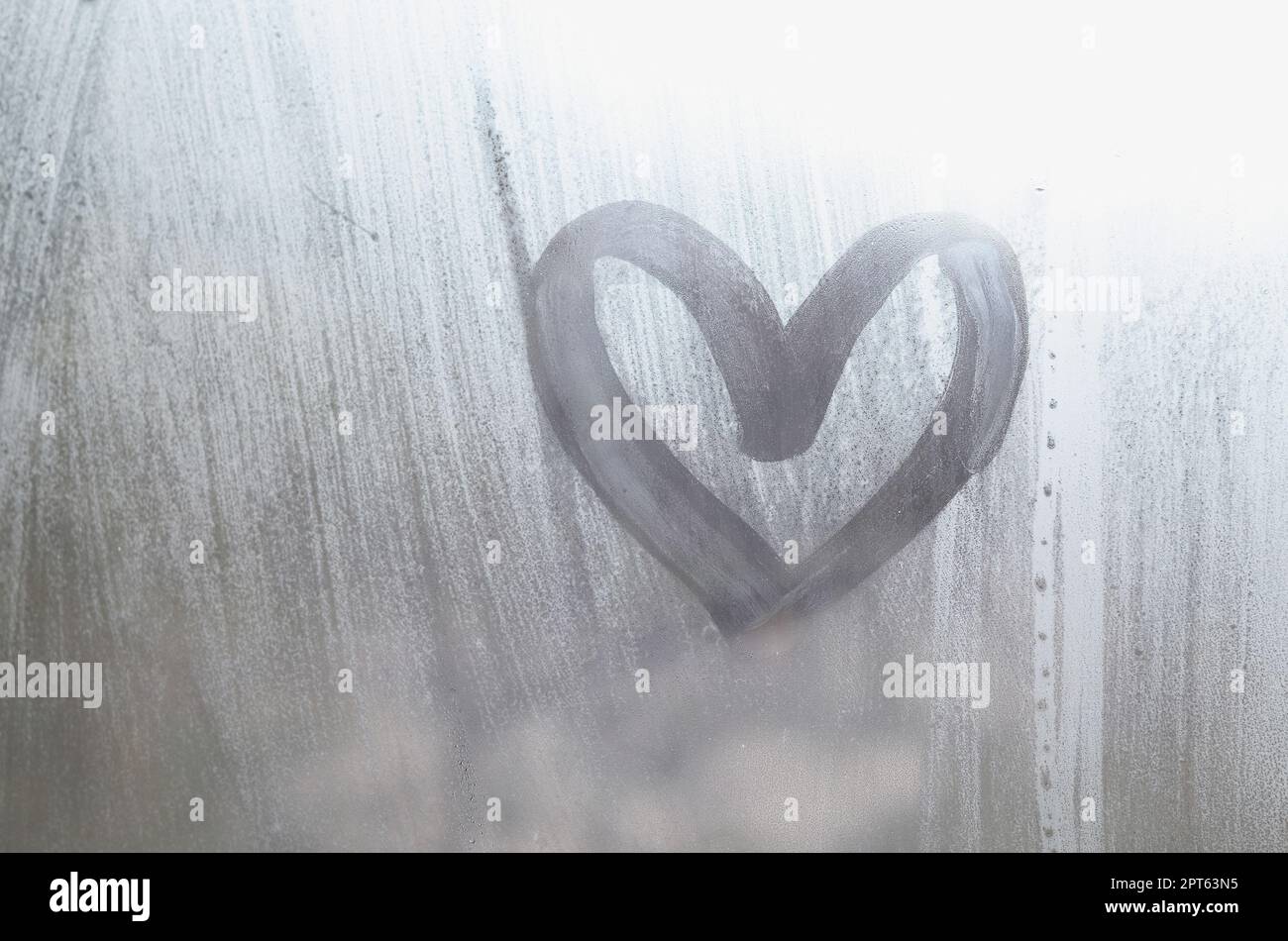 A heart-shaped drawing drawn by a finger on a misted glass in rainy ...