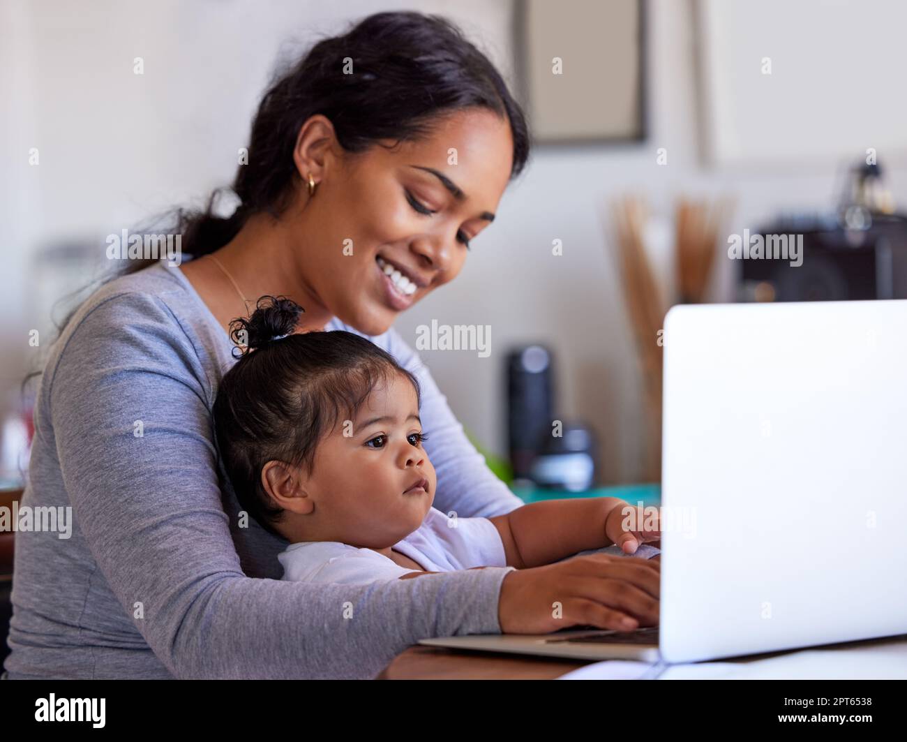 Working mother and baby at home, using a laptop. Young woman browsing ...