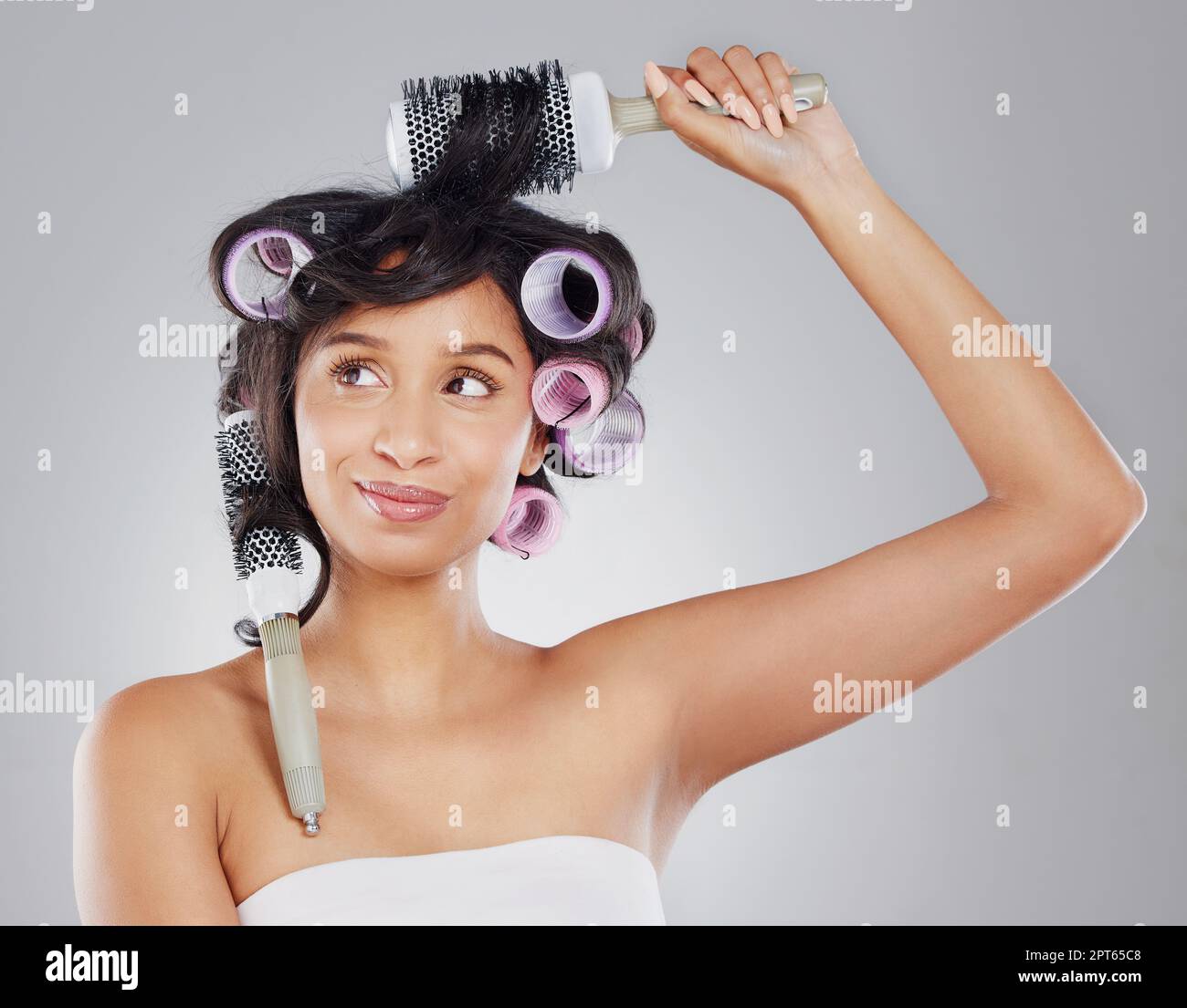 Add a little curl. an attractive young woman curling her hair against a ...