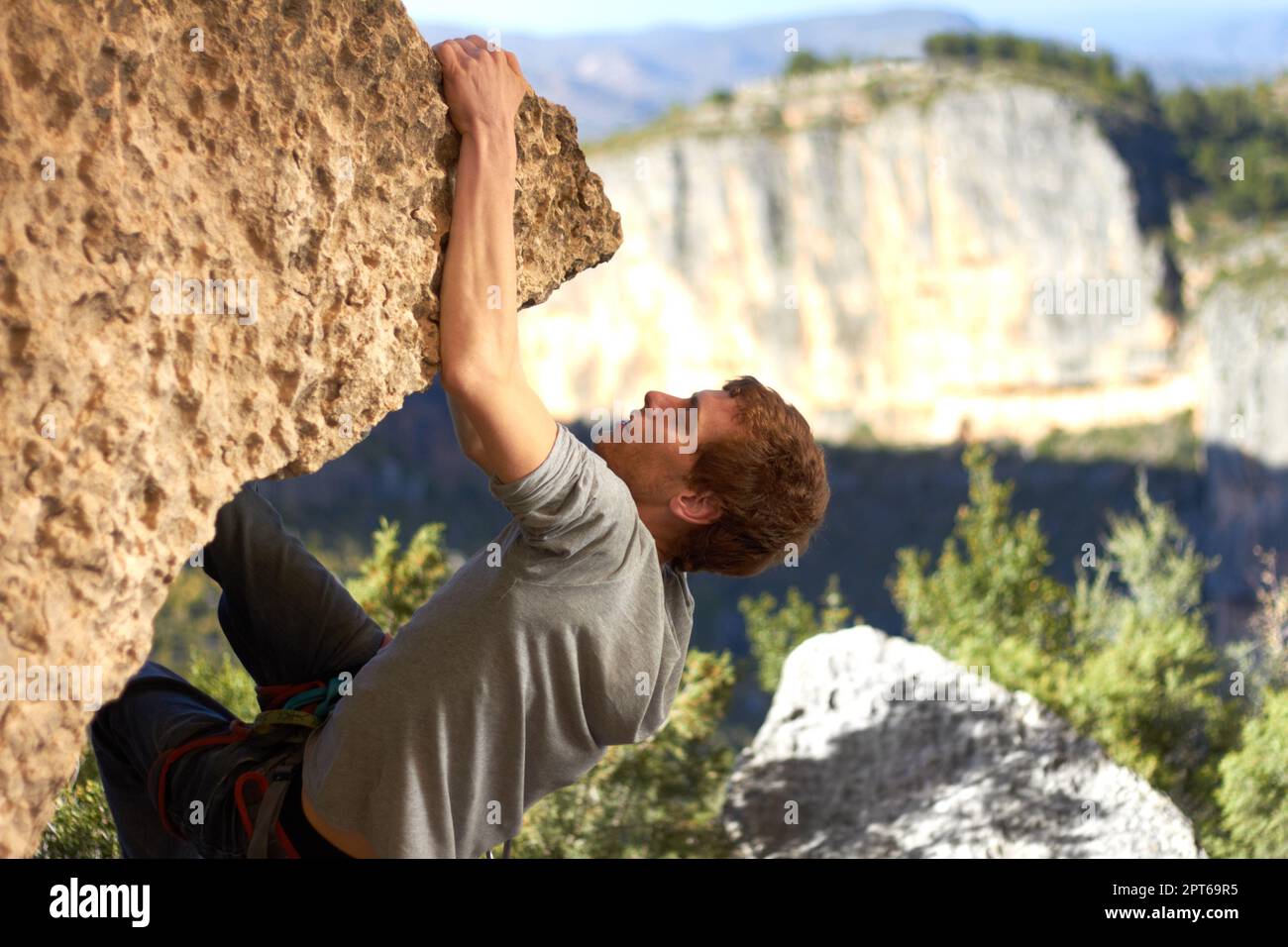 Hanging high. Profile of a rock climber dangling off the edge of a cliff with mountains in the ...
