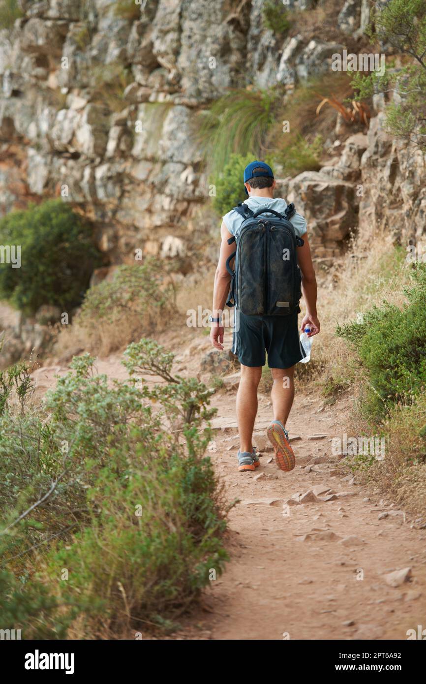 Wandering down a winding path. Rear-view of a young hiker walking down ...