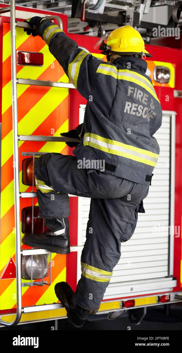 Manning the fire engine. a fireman climbing the ladder of his firetruck ...
