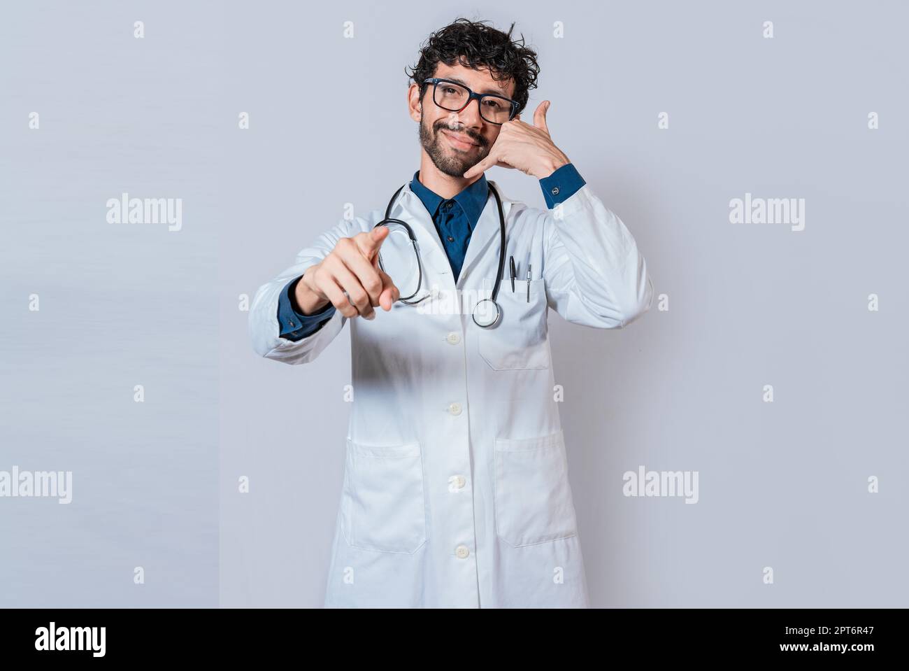 Smiling doctor making call gesture and pointing at the camera. Young ...