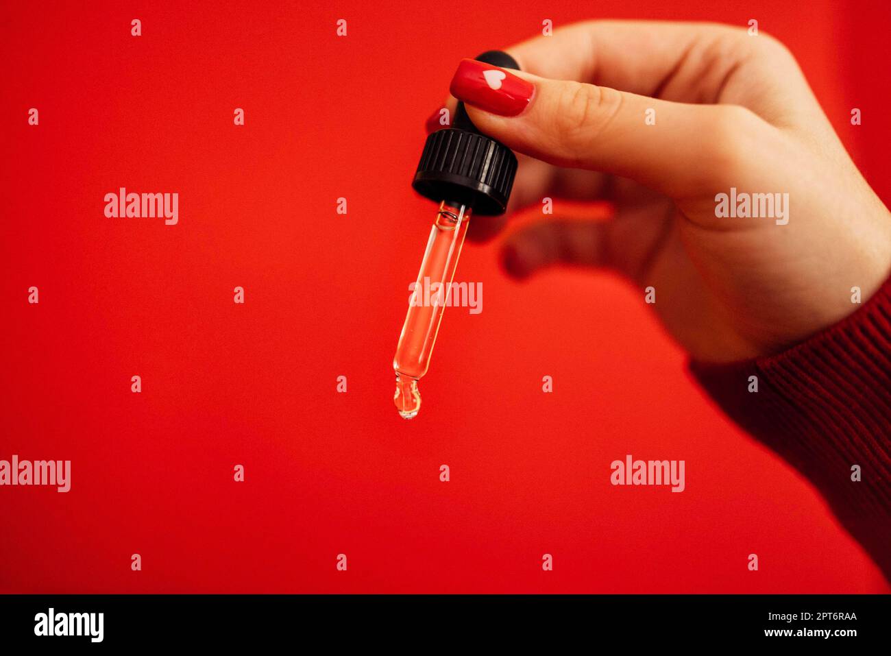 Woman with red manicure holding transparent serum or oil glass pipette ...
