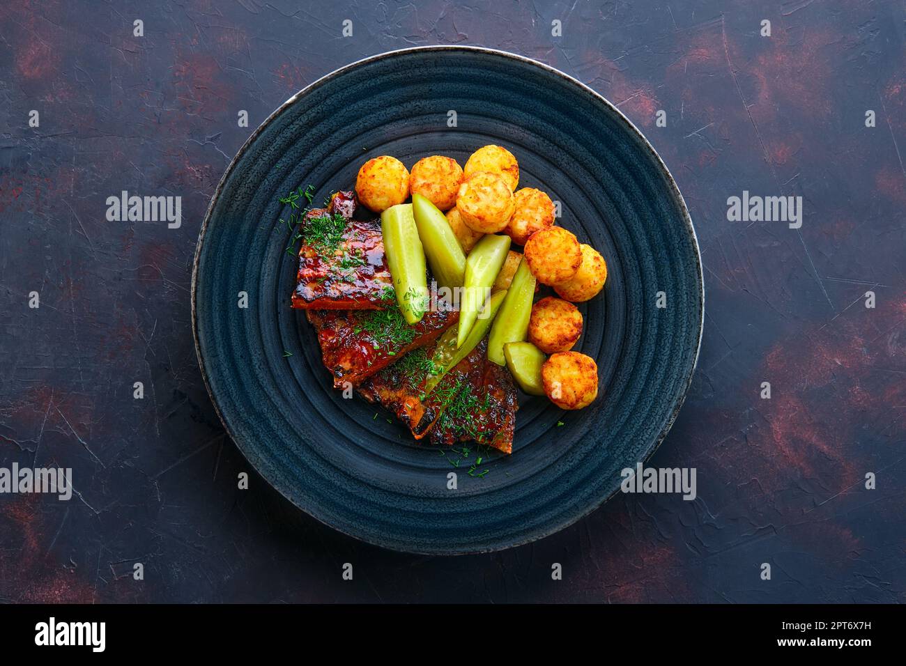 Top view of grilled ribs with pickled cucumber and fried potato balls ...