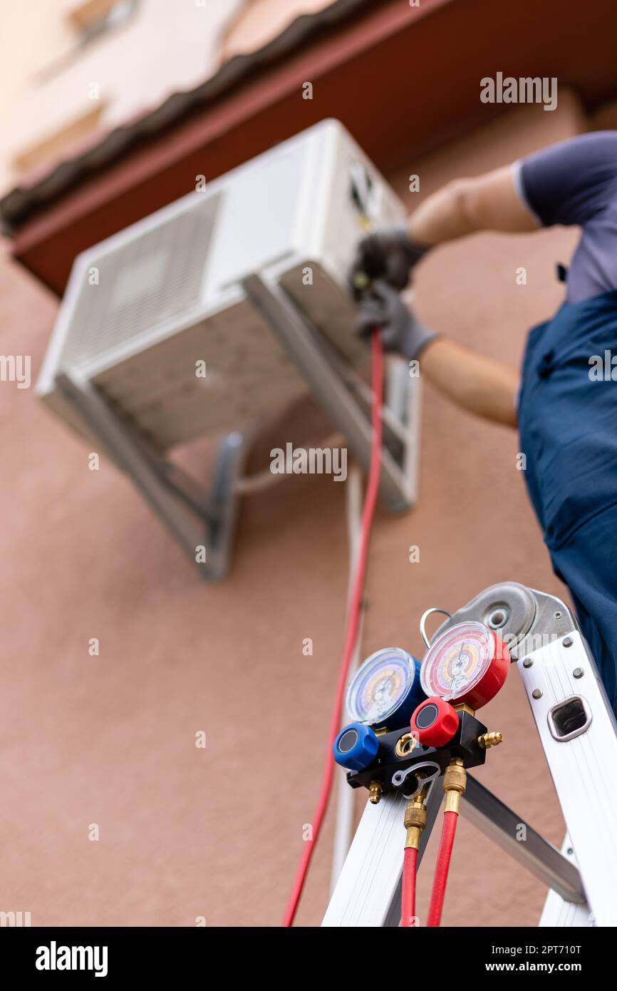 Worker maintains outdoor air conditioner using manometers for filling ...