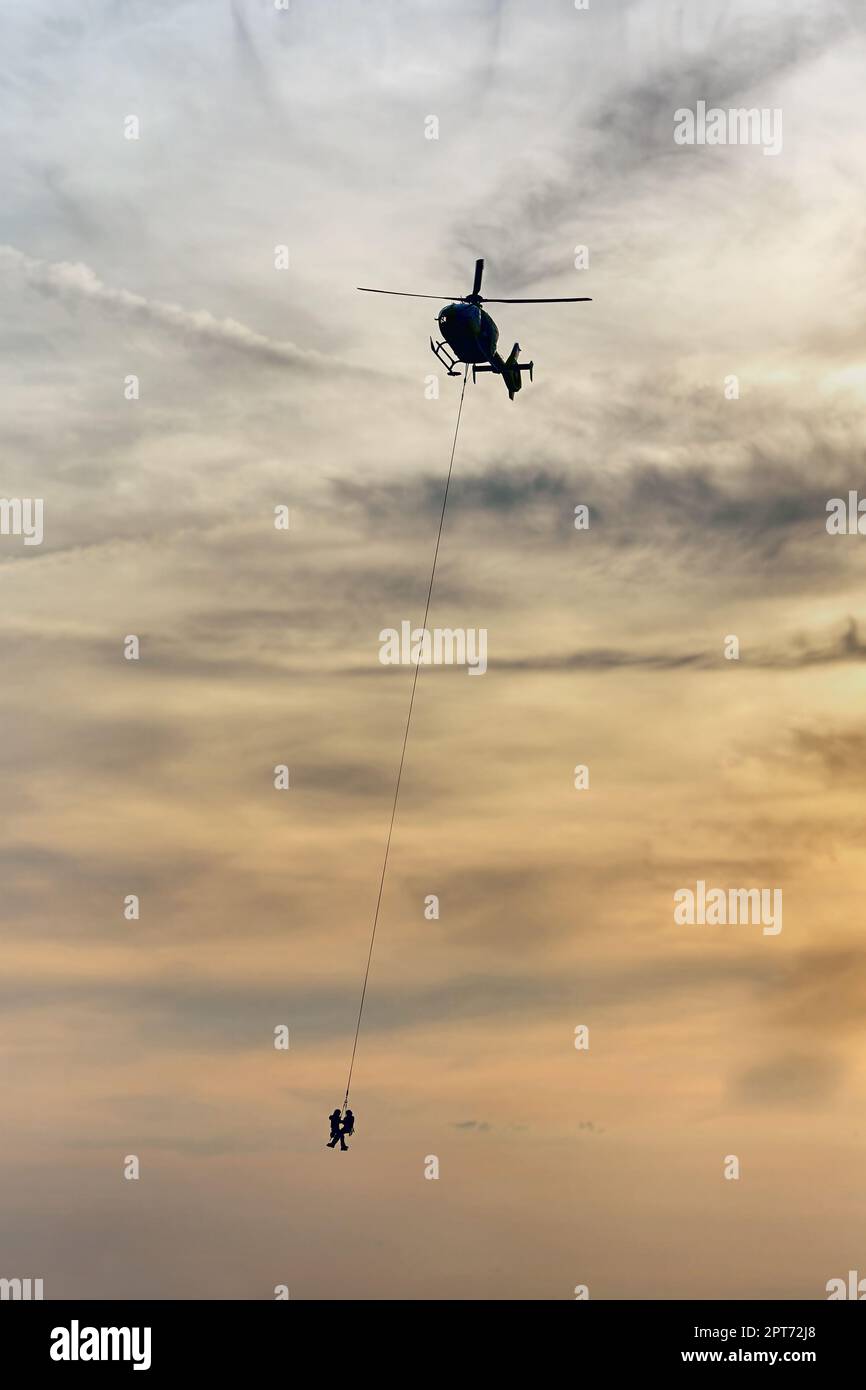 Rescue helicopter flying with people hanging from a rope Stock Photo ...