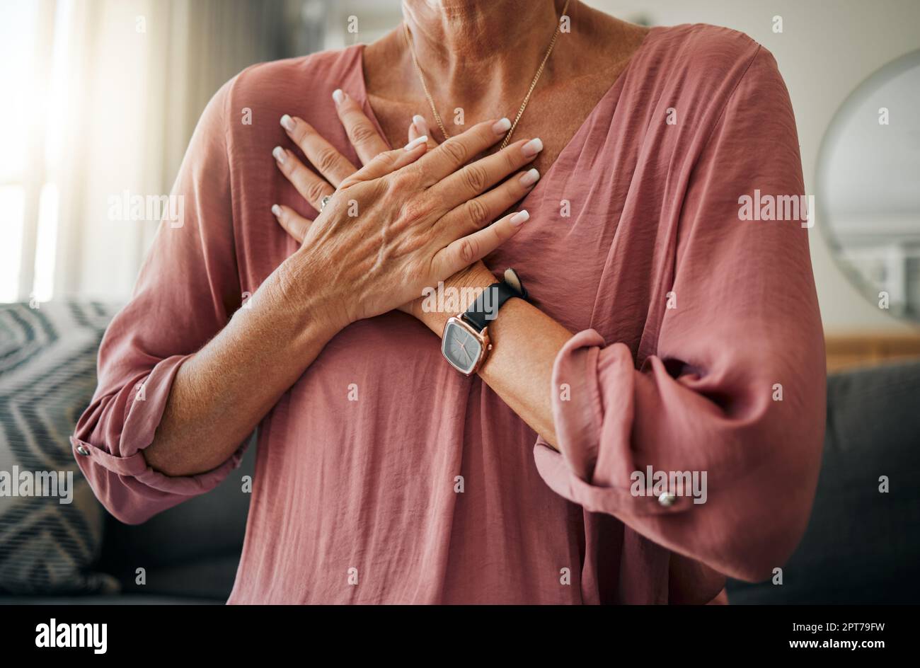 Senior woman, hands or chest pain in heart attack, anxiety or panic in house or home living room ...