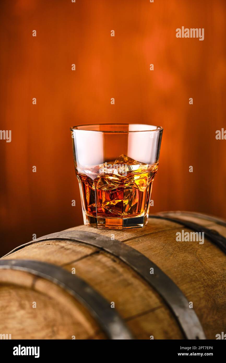 Glass of whisky with ice on the top of barrel (soft focus photo with ...