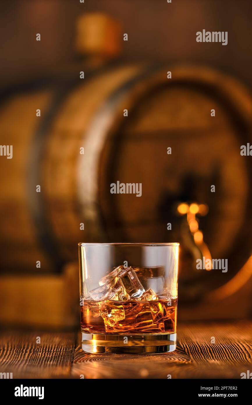 Glass of whisky with ice with barrel on background (soft focus photo ...