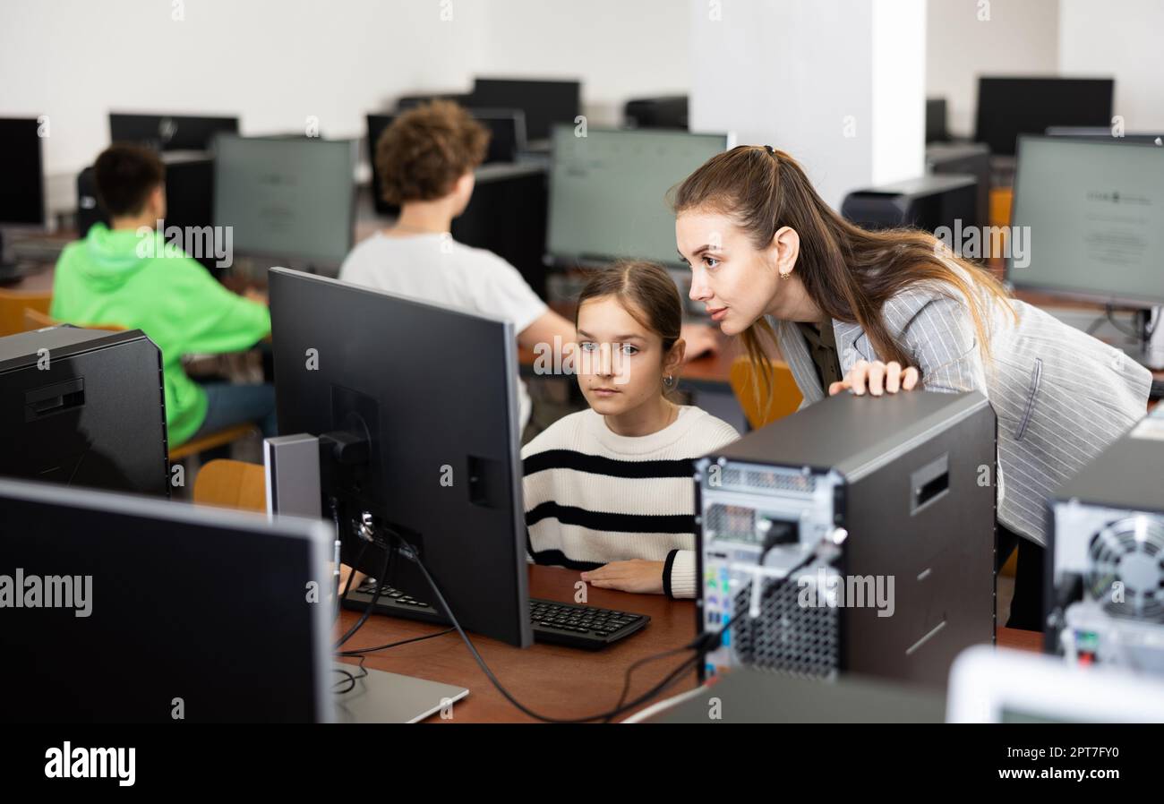 Female teacher talking to focused teen girl student in computer class ...