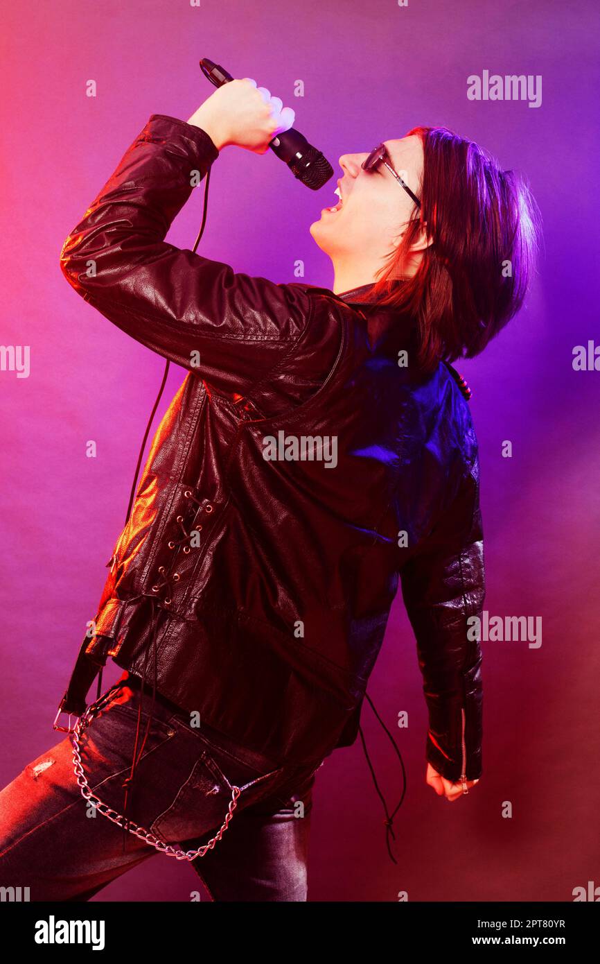 The young guy in leather jacket is singing in microphone on illuminated ...